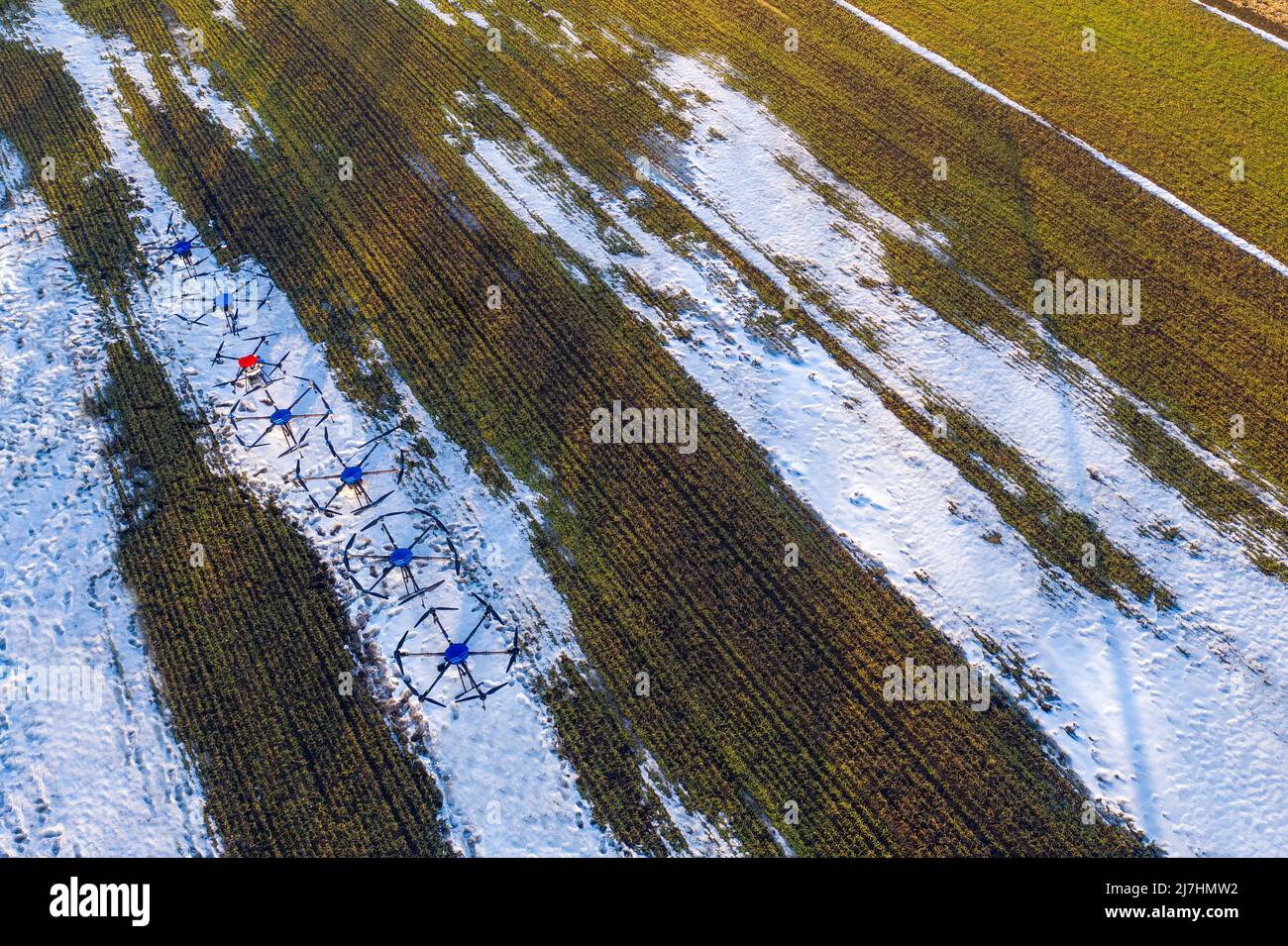 Many agrodrones are on the green field. The snow has not melted yet ...