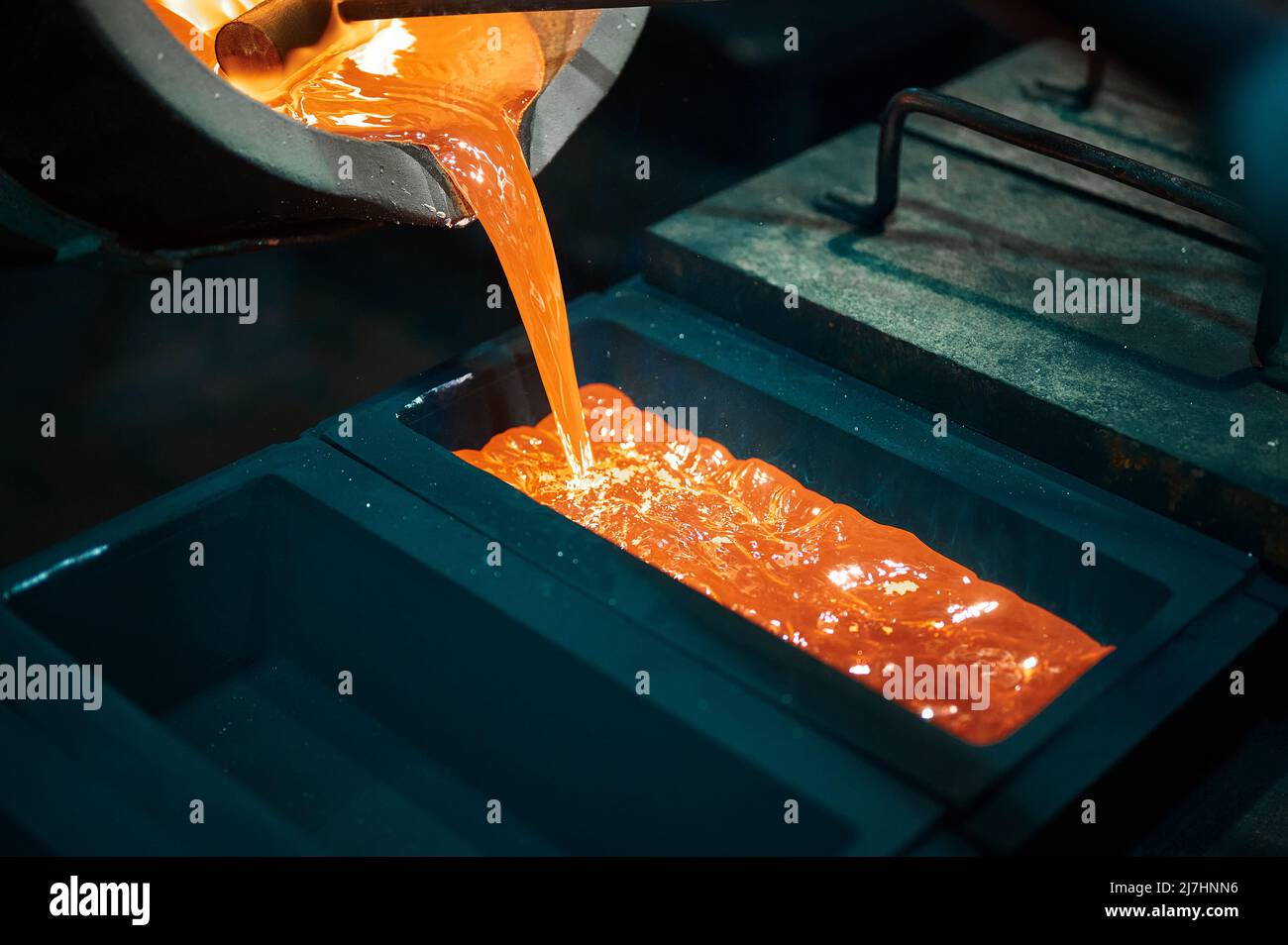 Pouring molten metal from a ladle into a rectangular graphite mold ...
