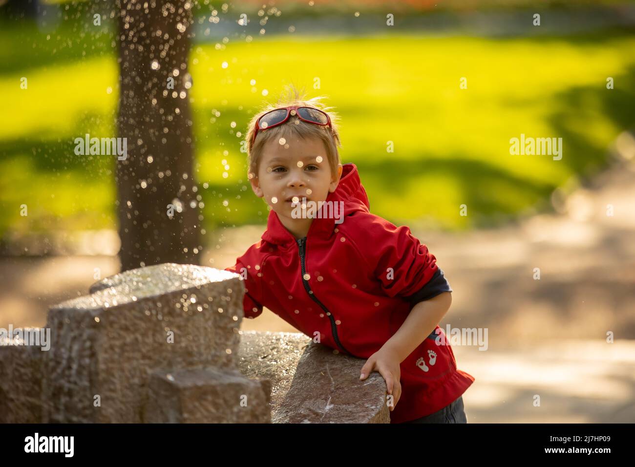 Cute toddler child, boy, splashing water from a fountain in the park ...
