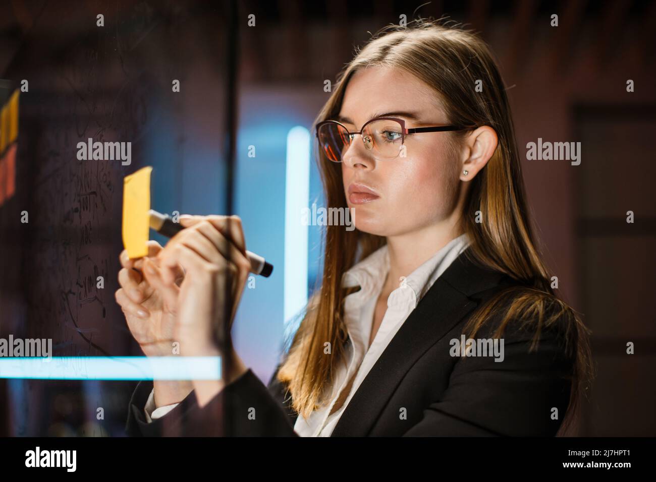 Young businesswoman writing tasks or creative ideas on sticky post it ...
