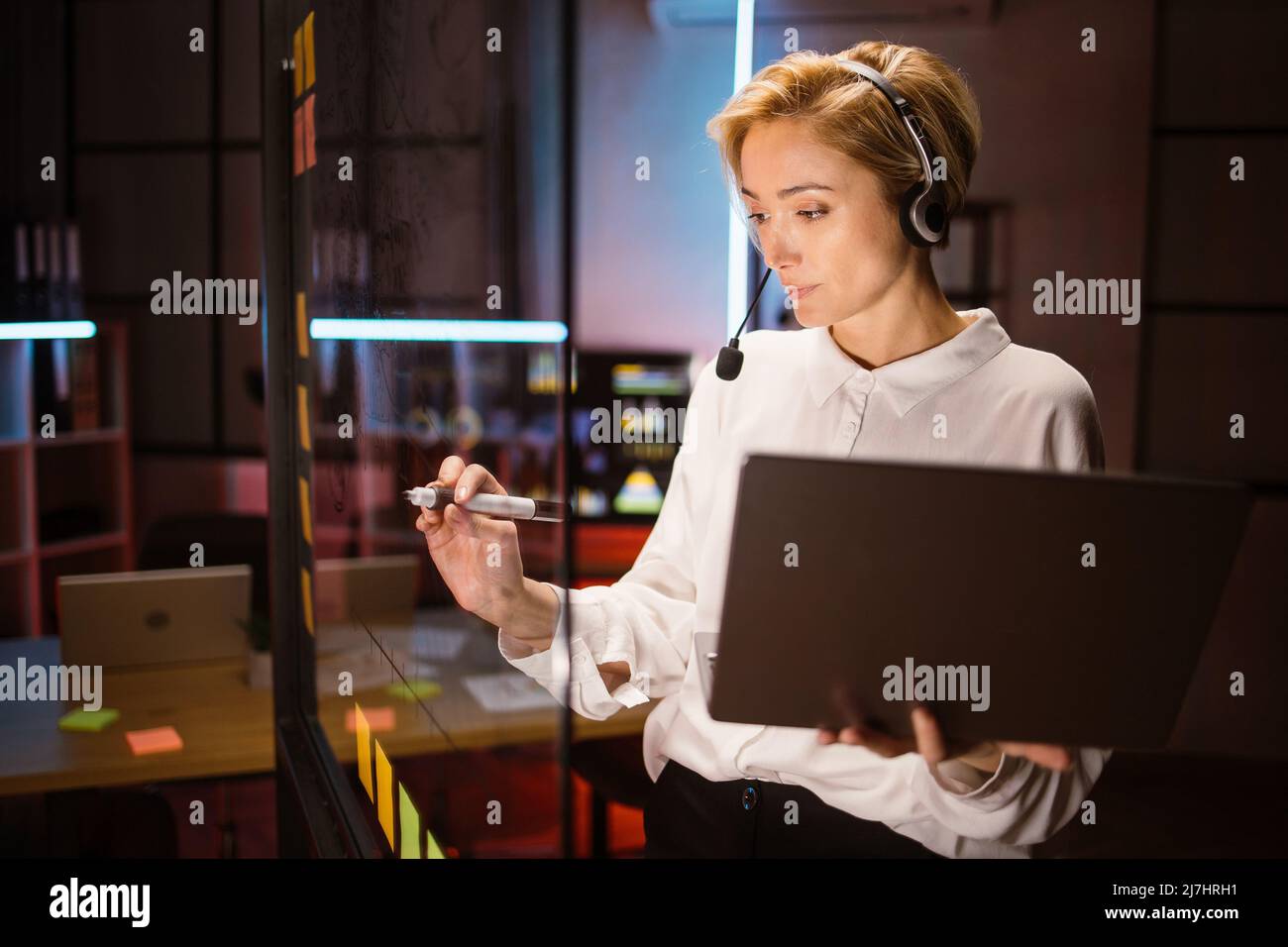 Side view of focused female worker, wearing headset and using laptop ...