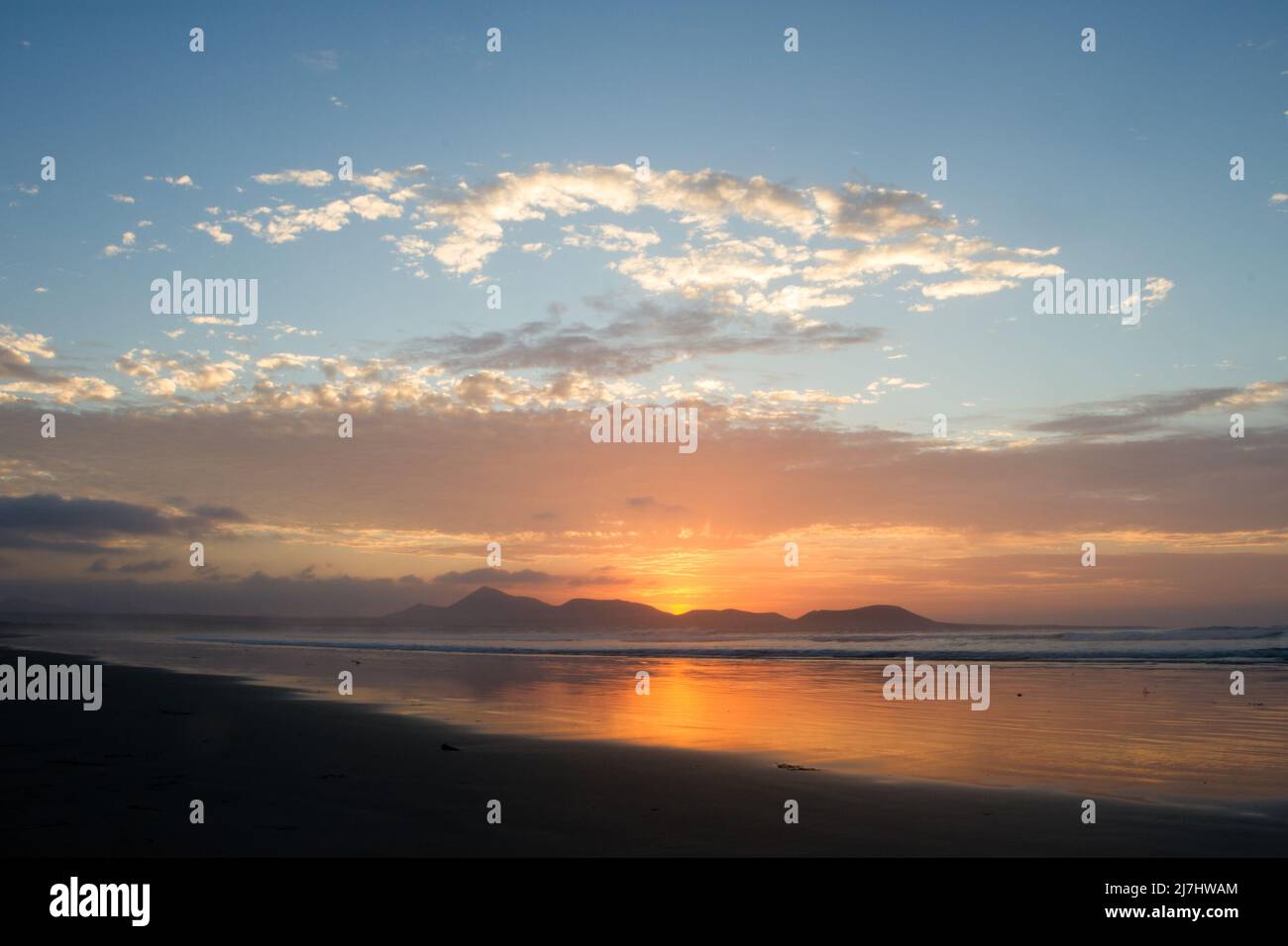 sunset at Famara beach, the sun's rays illuminate the clouds in red and ...