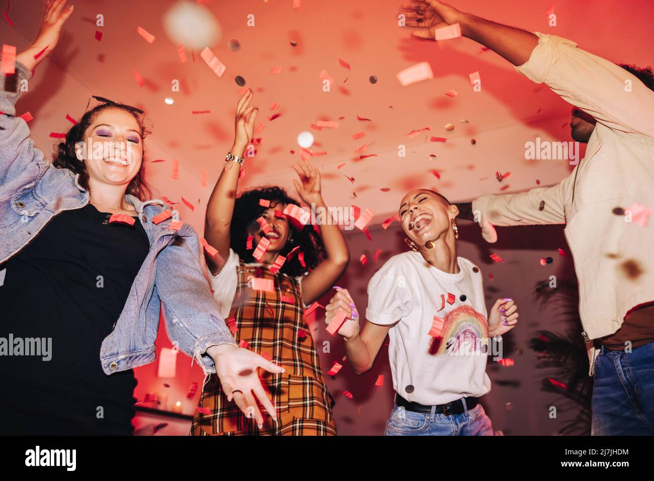 Happy friends dancing to their favourite song under falling confetti ...