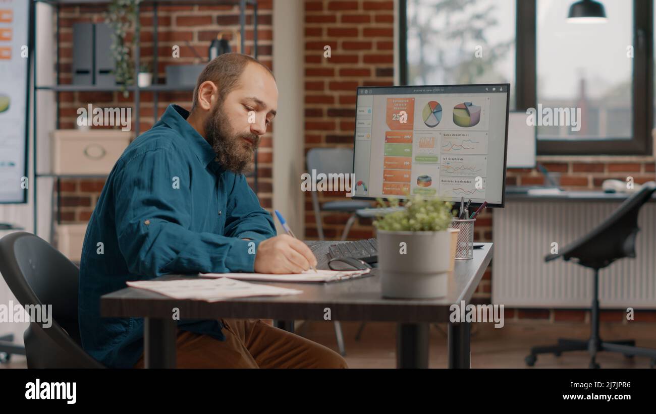 Employee analyzing rate charts on monitor and taking notes in startup ...