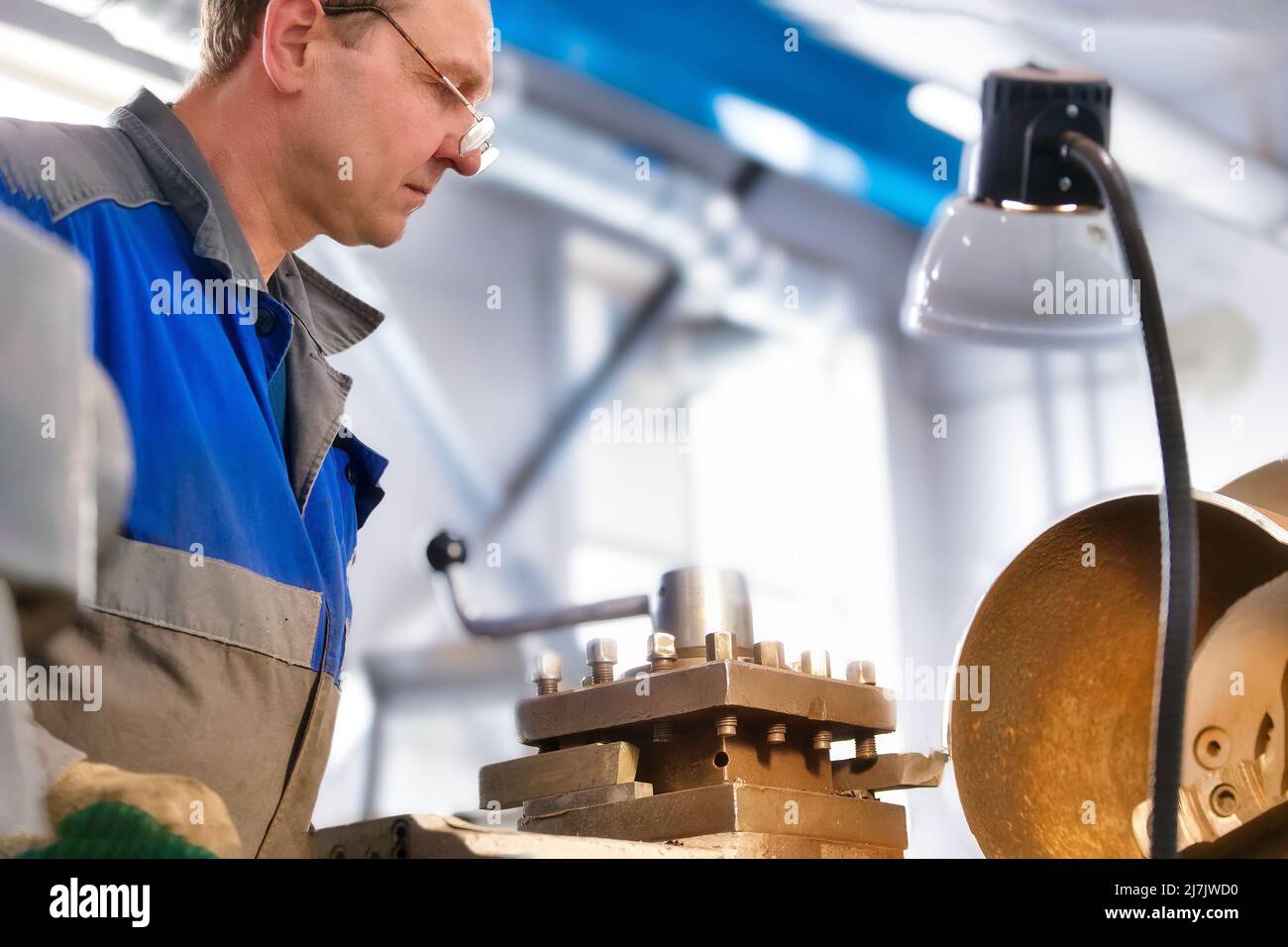Elderly turner of 50-55 years old in overalls works at lathe in ...