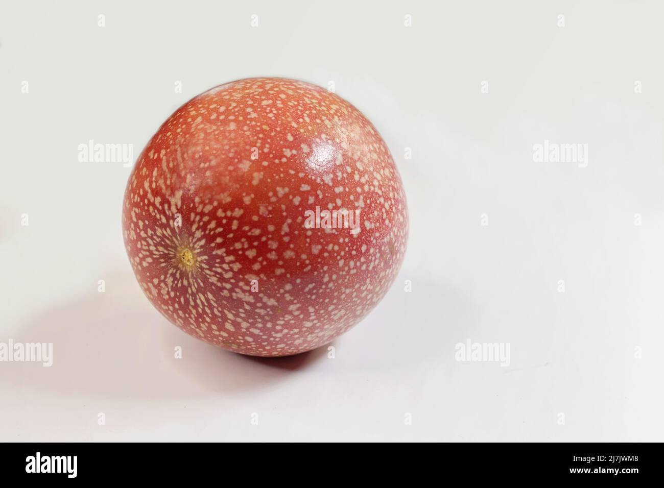 Close-up of a whole passion fruit with light pink red skin on white ...