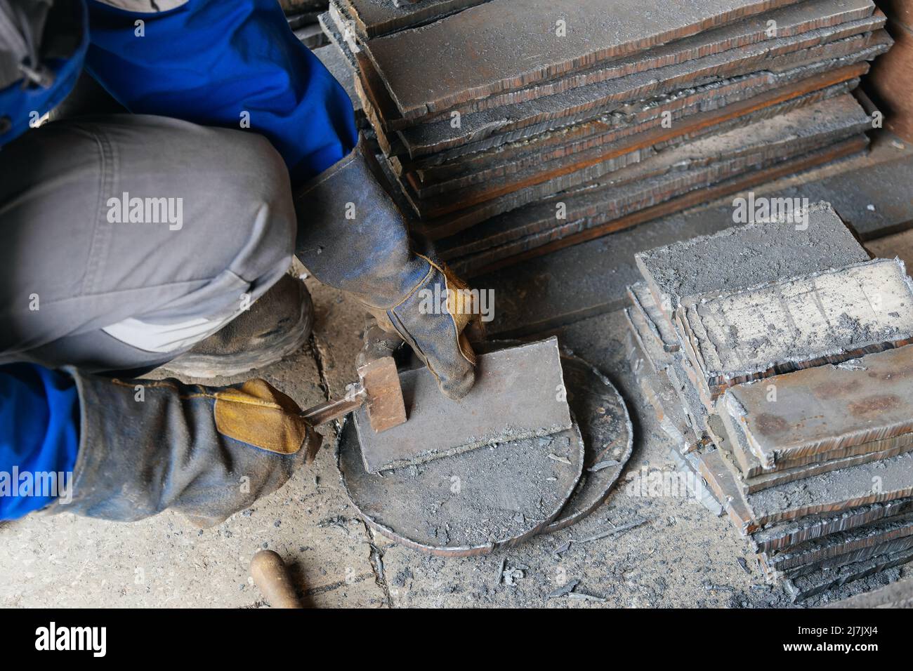 Worker in heavy industry or metallurgy beats scale off iron plates with ...