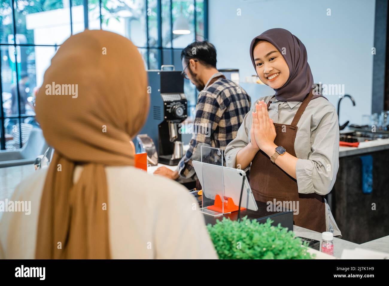 asian muslim cafe worker welcoming customer at her shop Stock Photo - Alamy