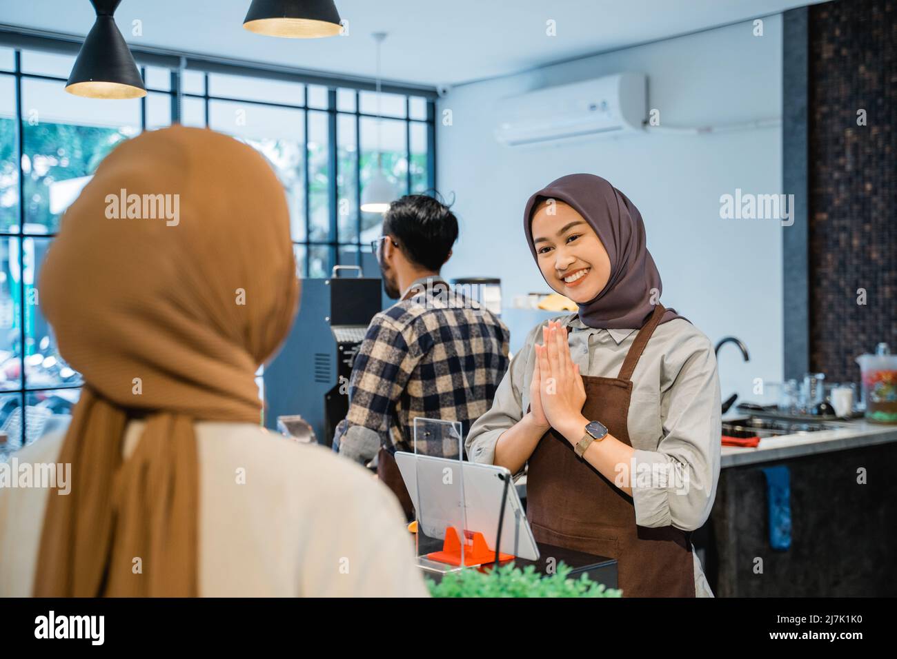 asian muslim cafe worker welcoming customer at her shop Stock Photo - Alamy