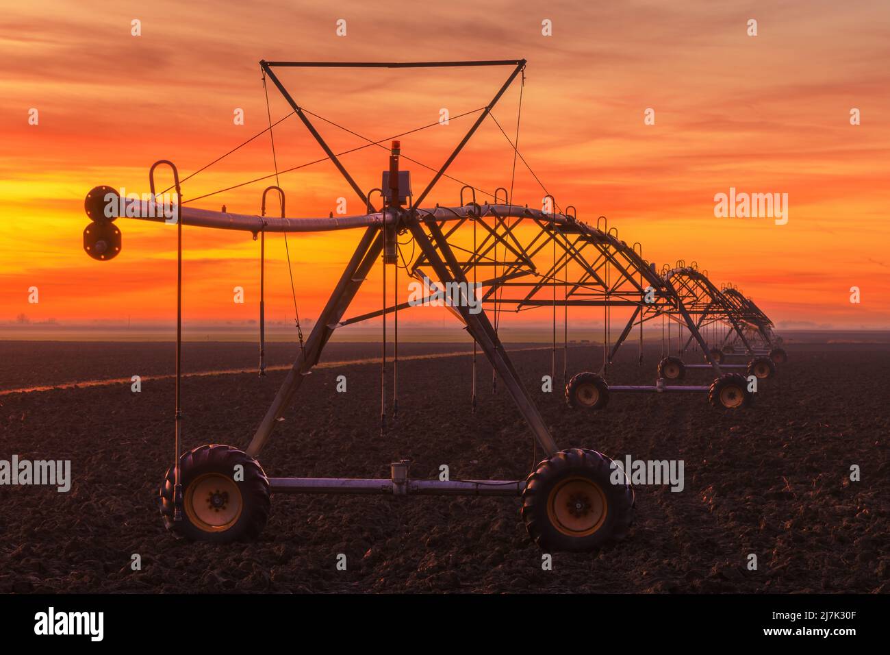 Lateral move agricultural irrigation system on plowed field in sunset ...
