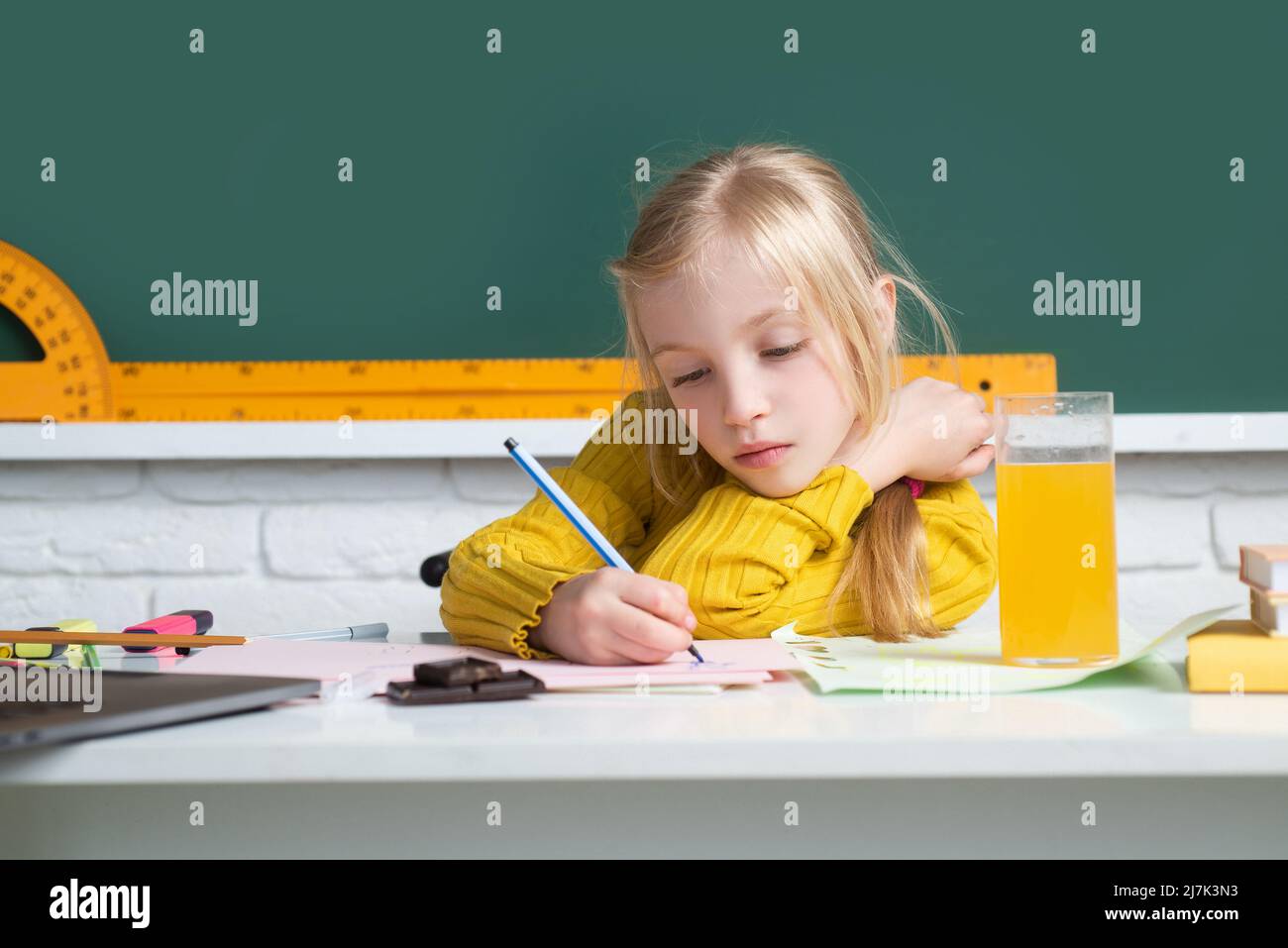 Portrait of cute little schoolgirl writing in book with classmates in ...