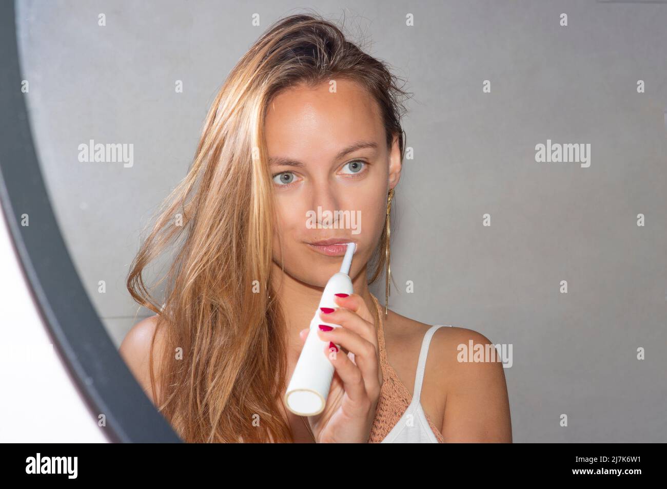 pretty blonde woman brushing her teeth with an electric toothbrush ...