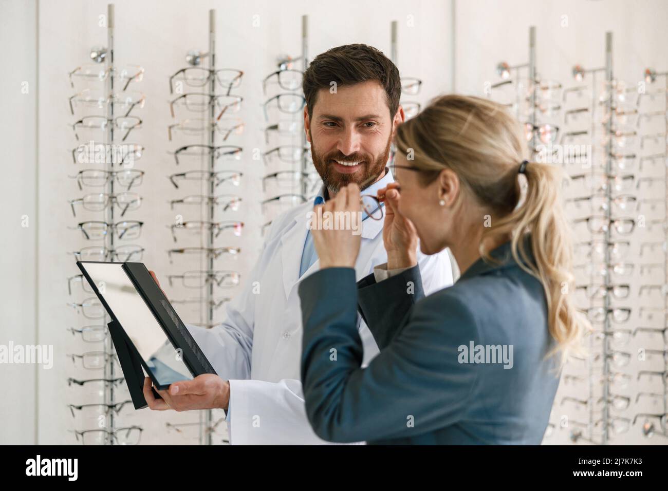 Smiling optometrist helping woman to choose glasses in optical store ...