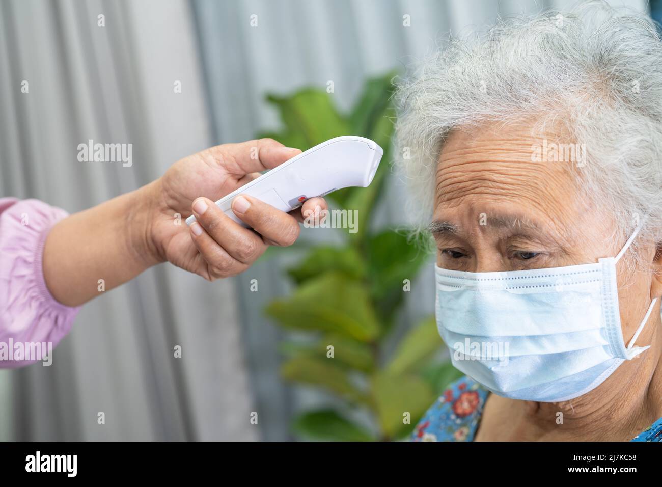 Caregiver holding digital thermometer to measures asian senior or ...