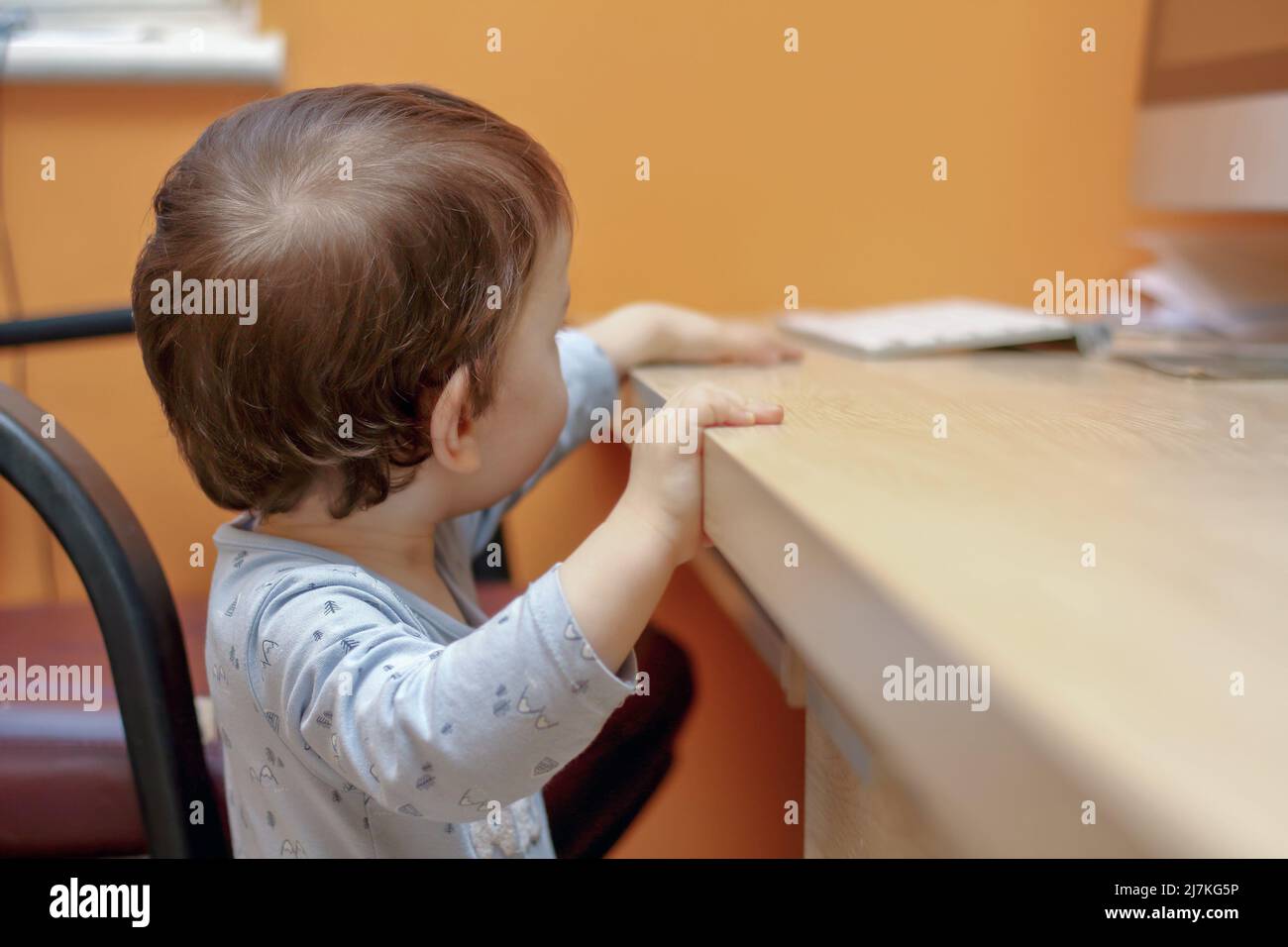 A one-year-old boy reaching for the keyboard lying on the desk Stock ...