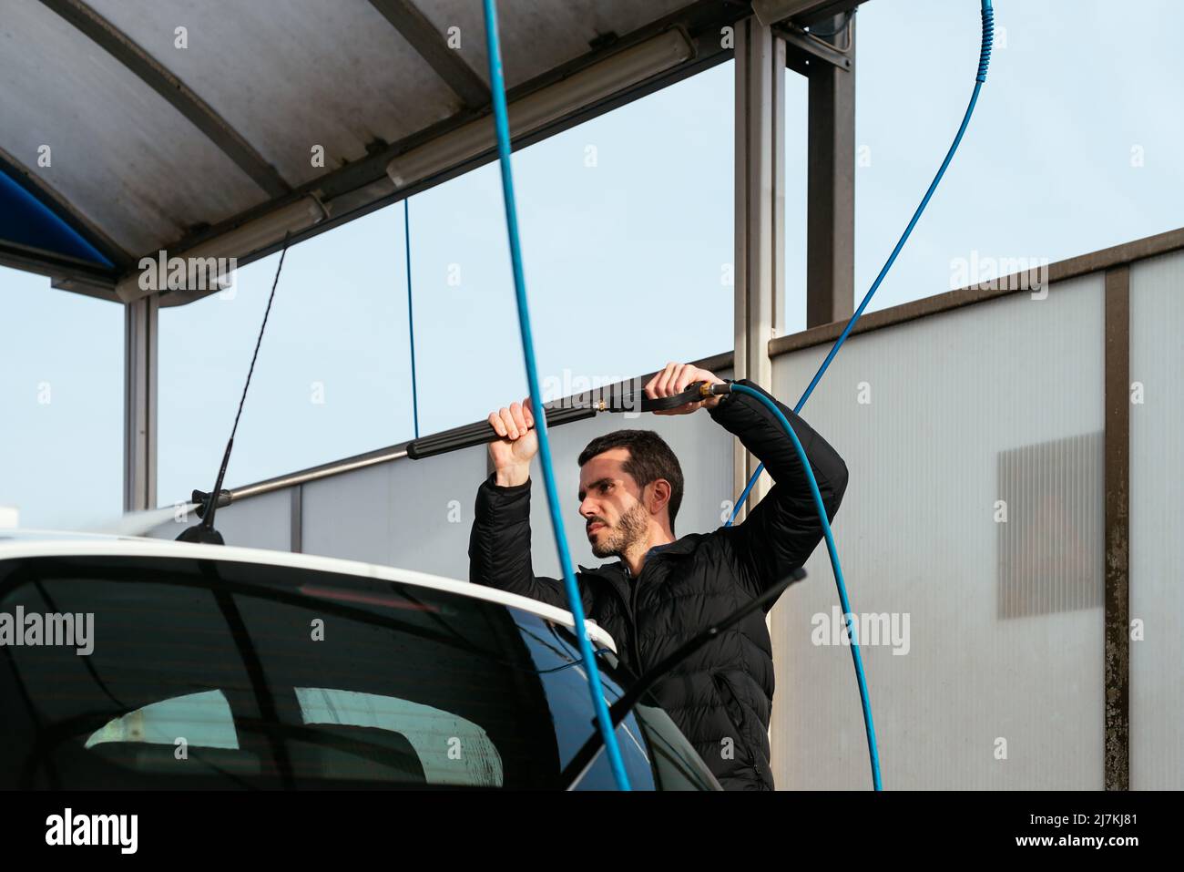 Focused man with hose washing car at washing station Stock Photo - Alamy