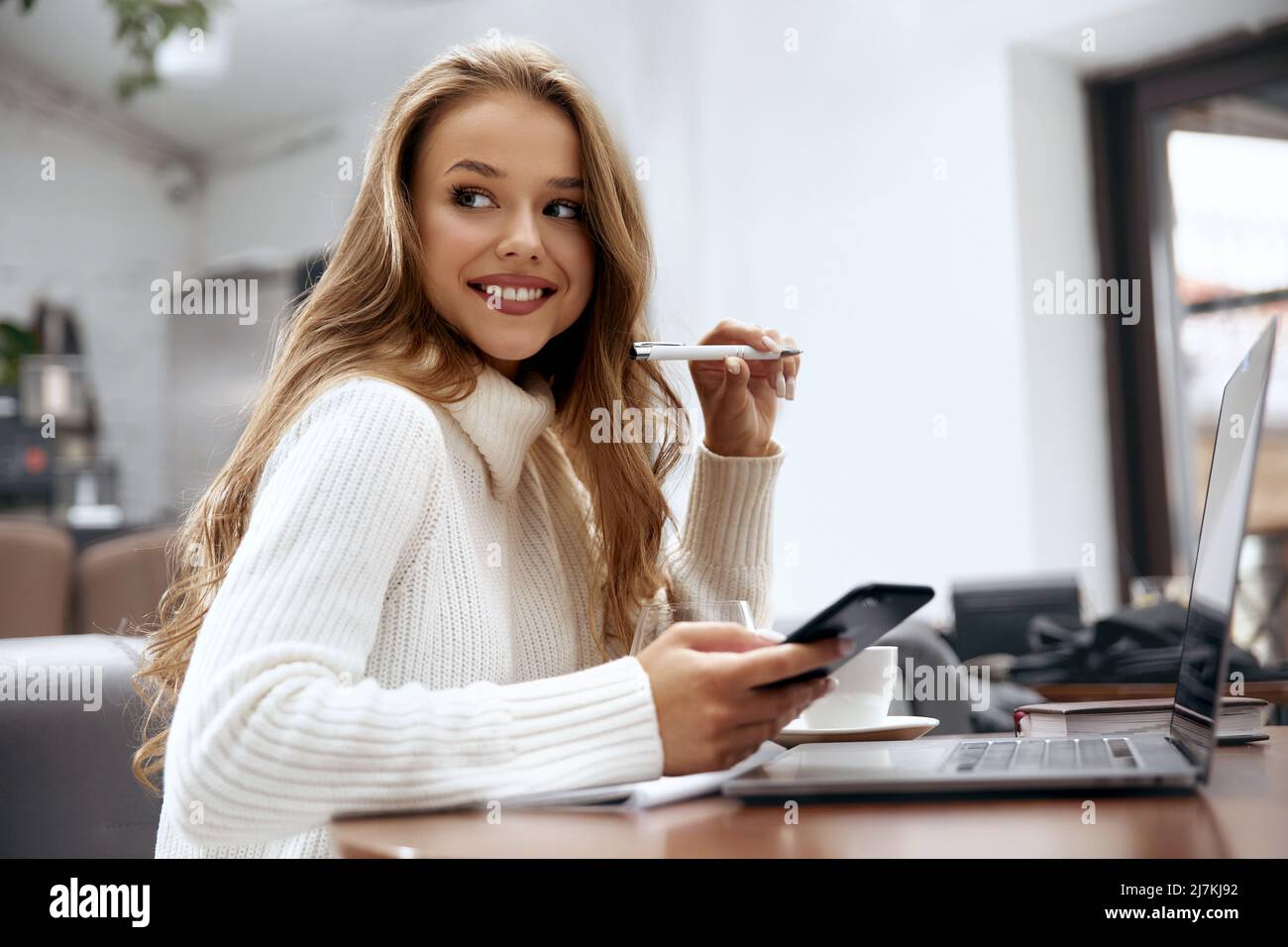 Beautiful young woman in casual clothing using laptop and smiling while ...