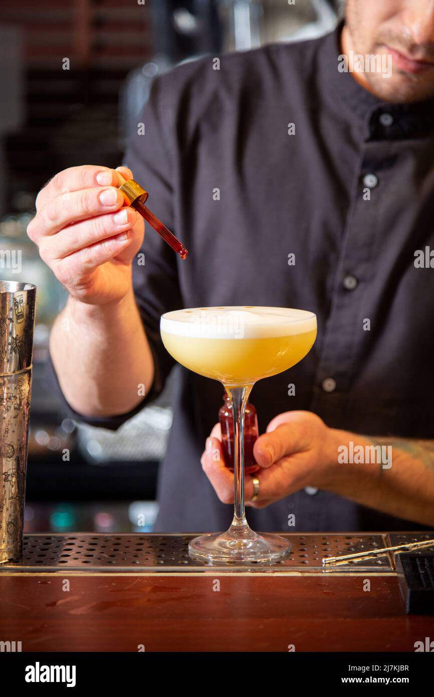 Crop unrecognizable male barkeeper adding syrup with pipette into glass ...