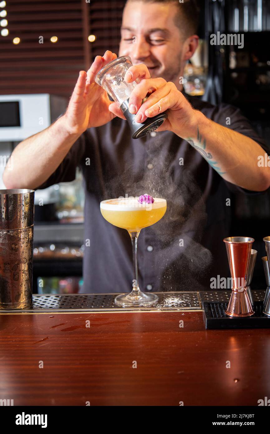 Crop positive young male barkeeper adding powder on glass of refreshing ...
