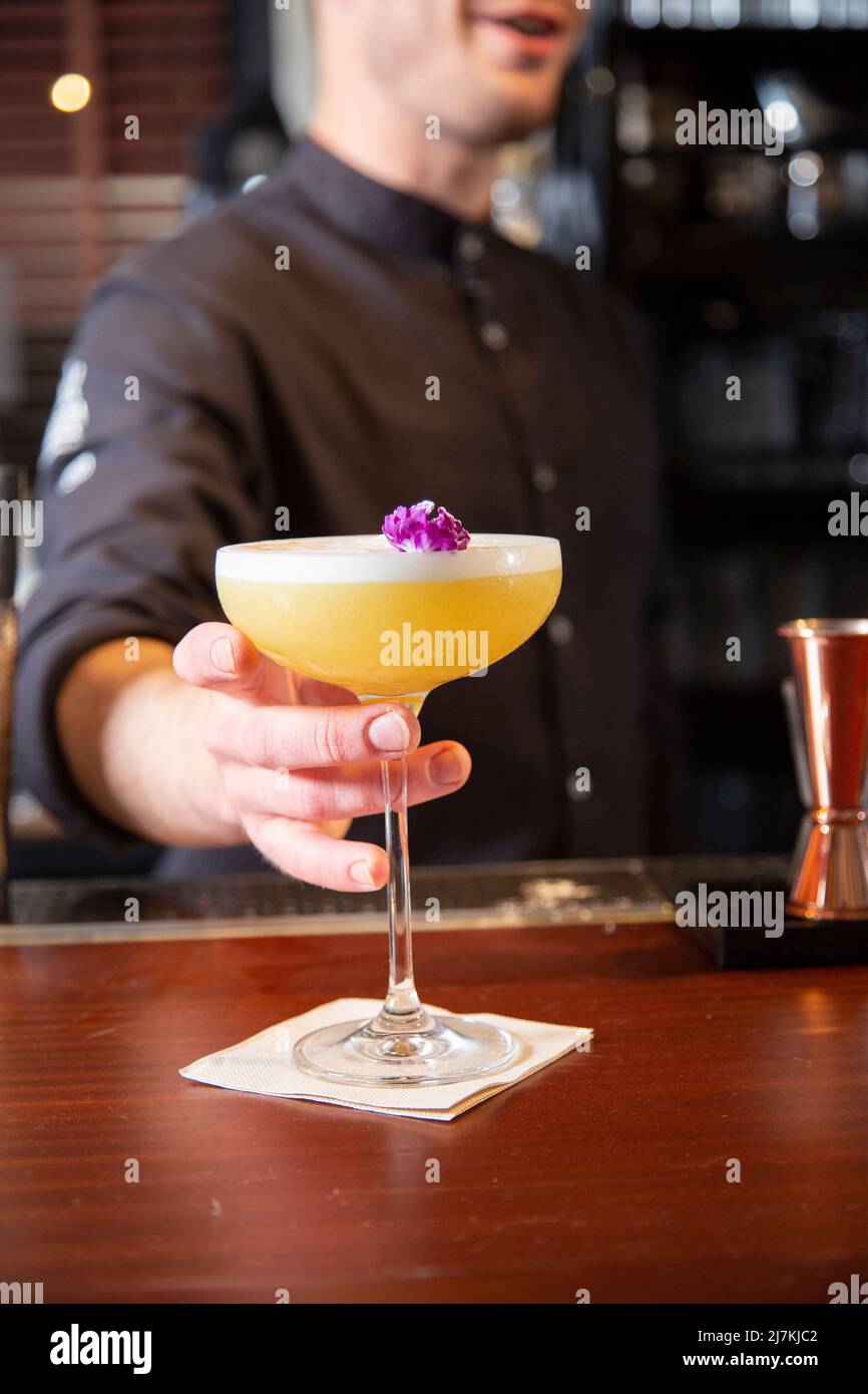 Crop friendly young male barkeeper in uniform serving delicious sour ...