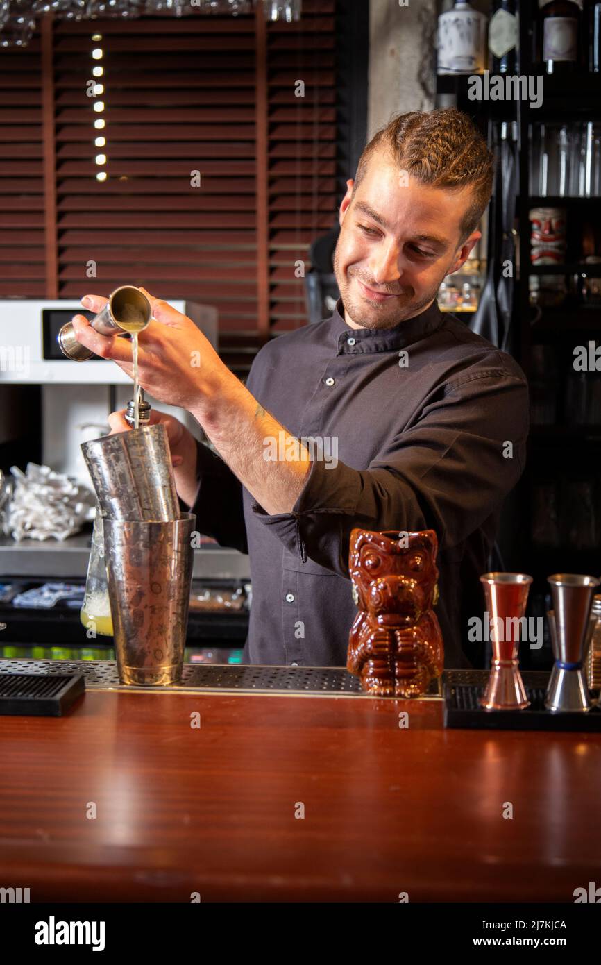 Cheerful young professional barman in uniform pouring orange juice from ...