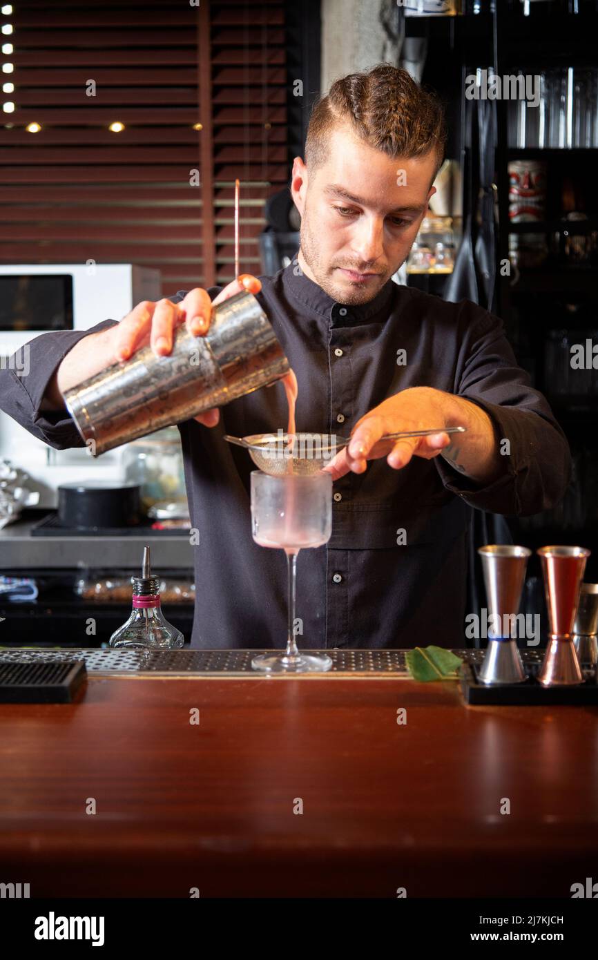 Concentrated young male bartender in black uniform pouring exotic ...
