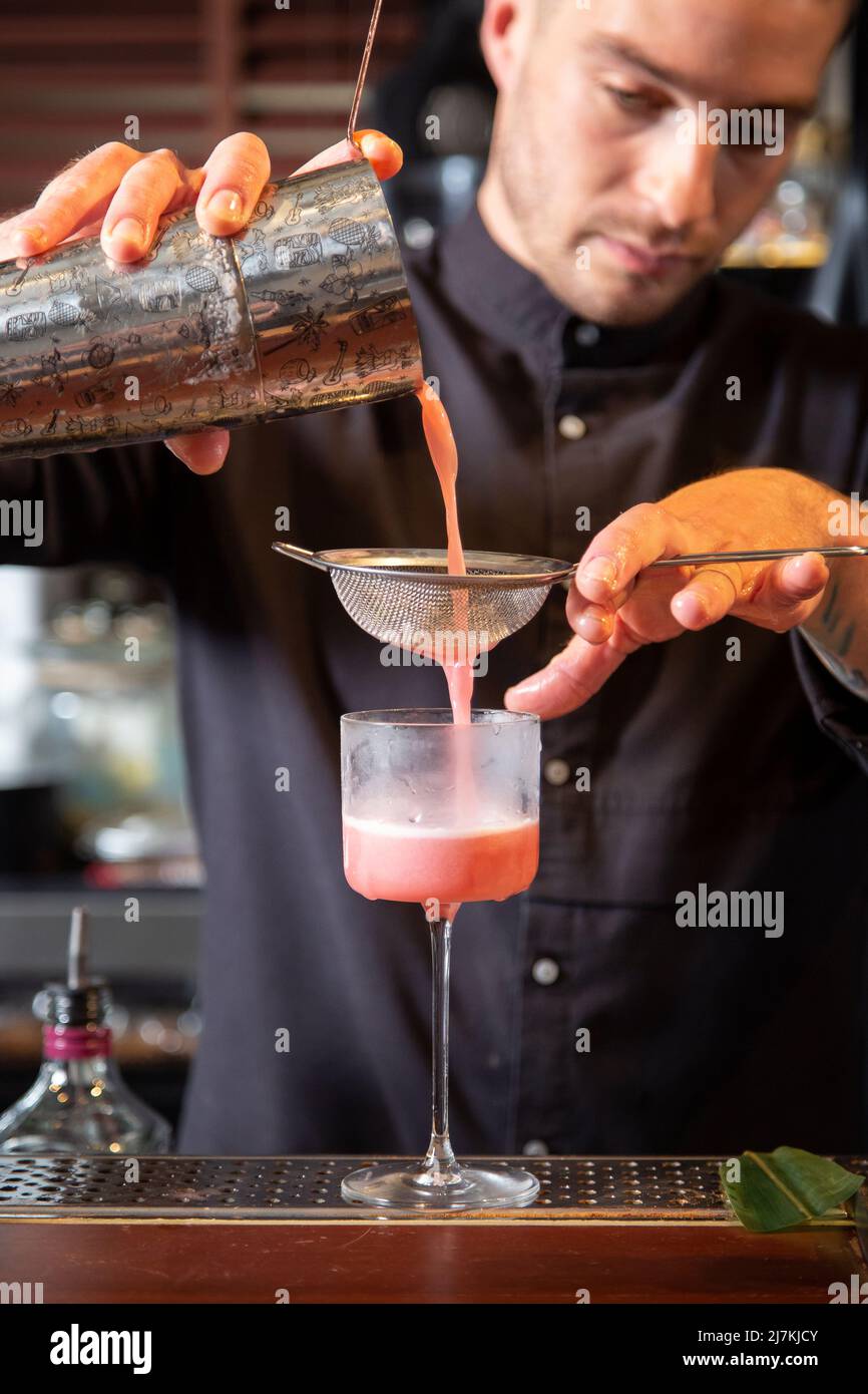 Concentrated young male bartender in black uniform pouring exotic ...