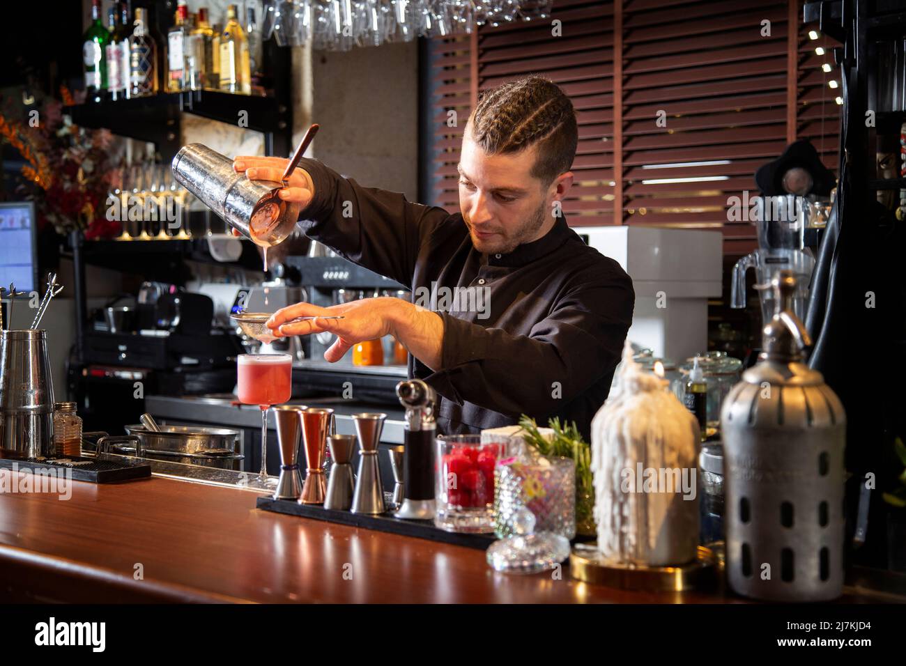 Concentrated young male bartender in black uniform pouring exotic ...