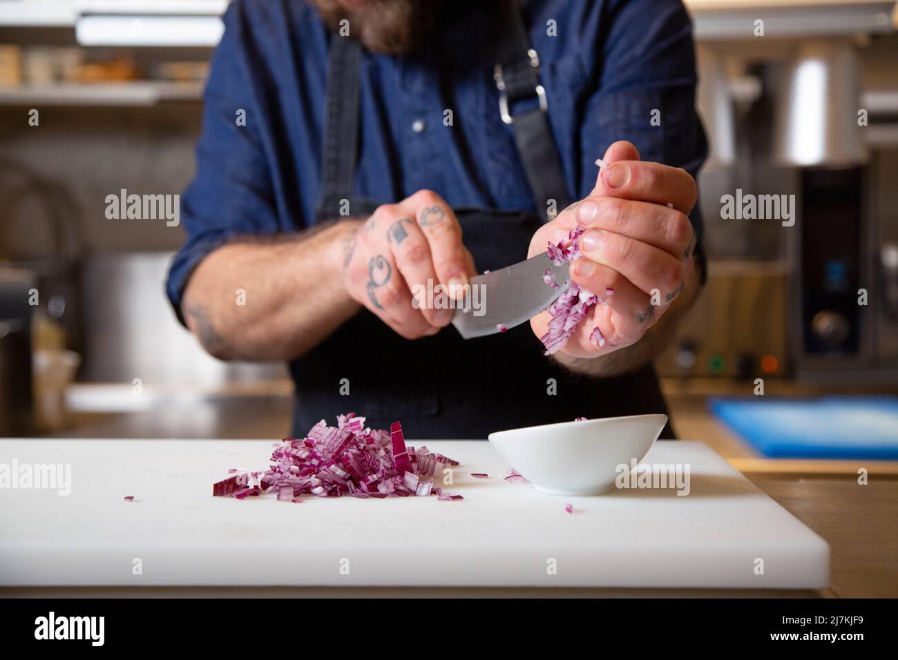 Crop unrecognizable tattooed male chef in apron putting chopped red ...