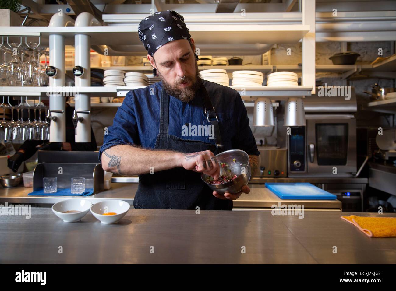 Concentrated male cook in uniform mixing fresh ingredients into bowl at ...