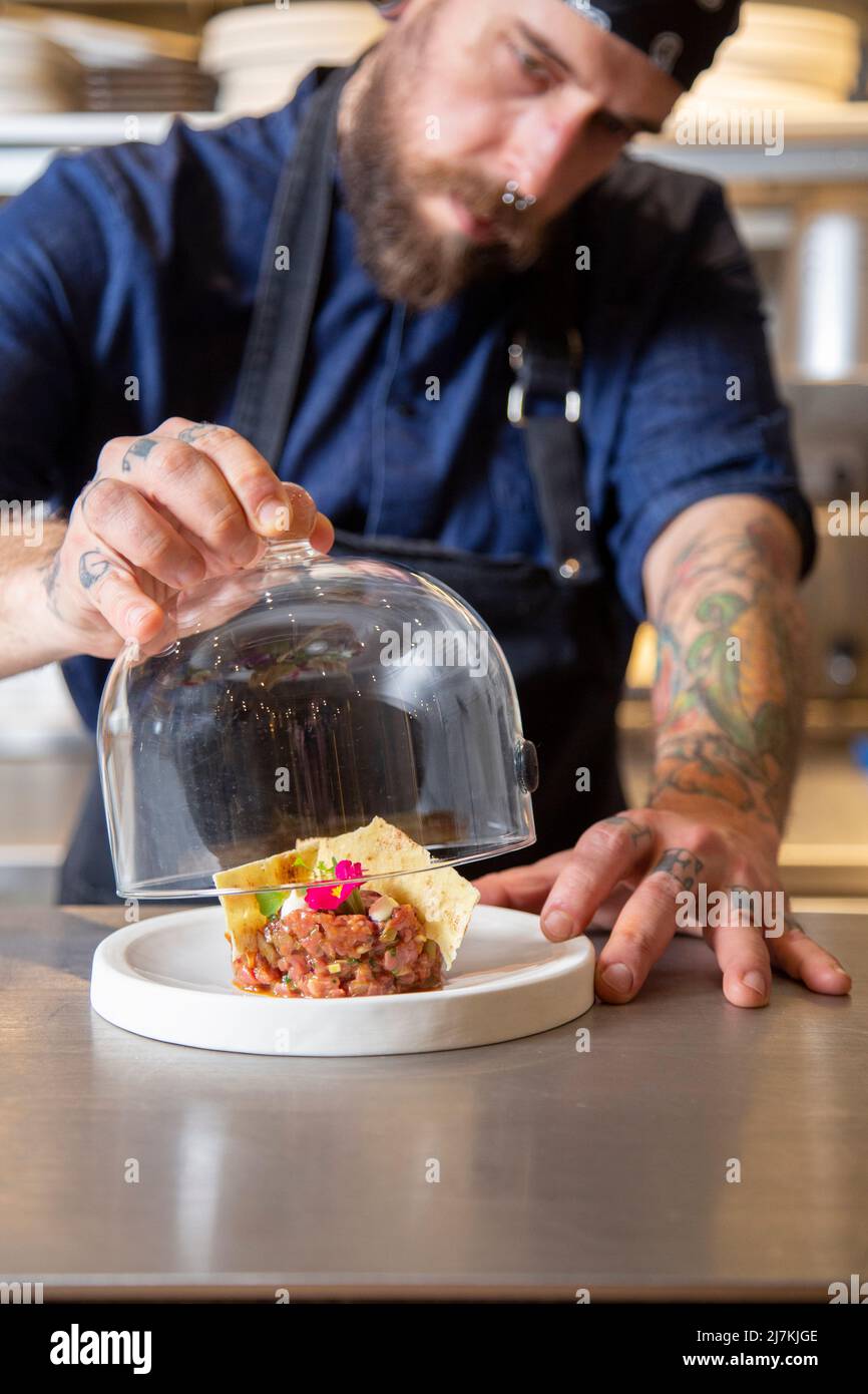 Crop focused male chef in uniform covering fresh tasty tartare with ...