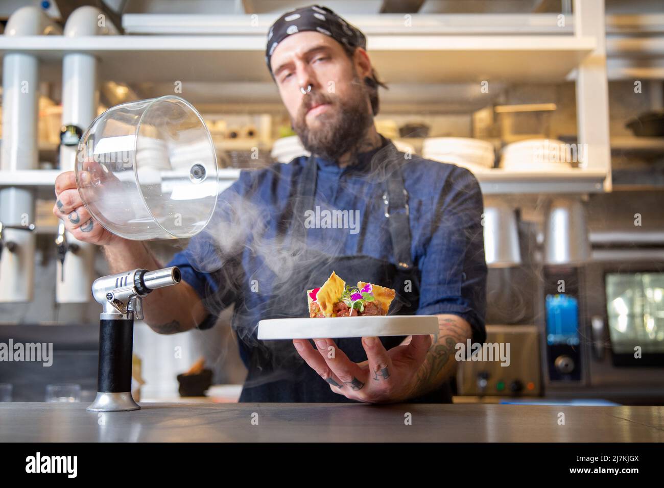 Serious bearded male chef looking at camera while using smoking gun and ...