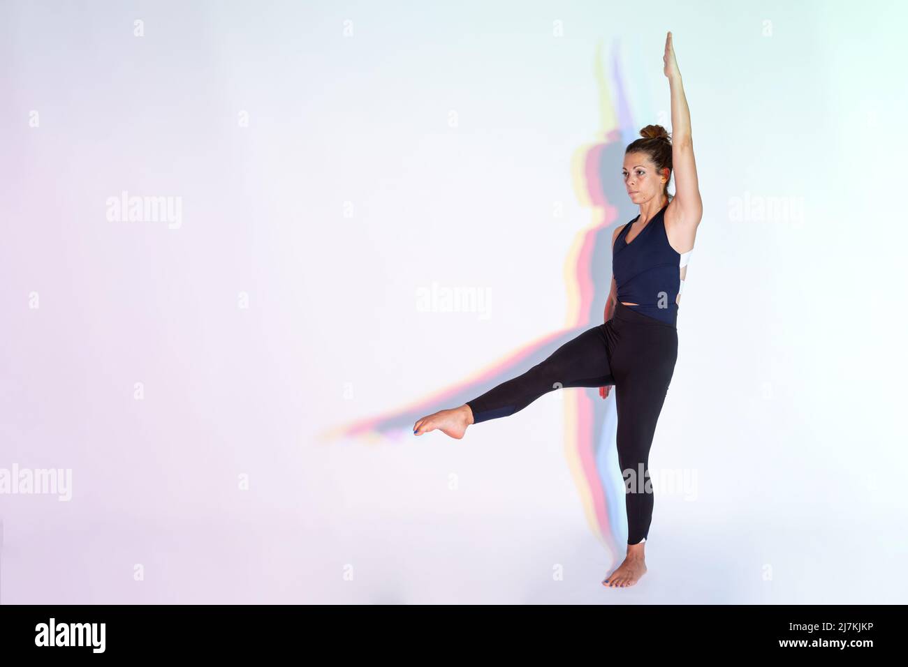 Full body of active barefoot female standing on one leg with raised arm ...