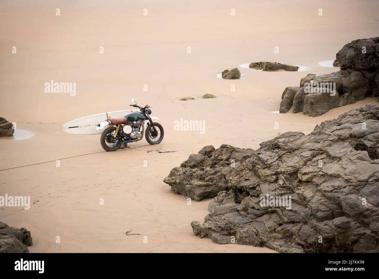 From above of motorcycle with surfboard attached parked on sandy beach ...