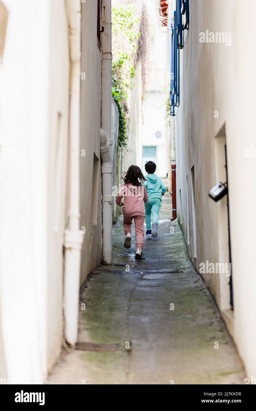 Anonymous girl in pink clothes chasing boy while running on narrow ...