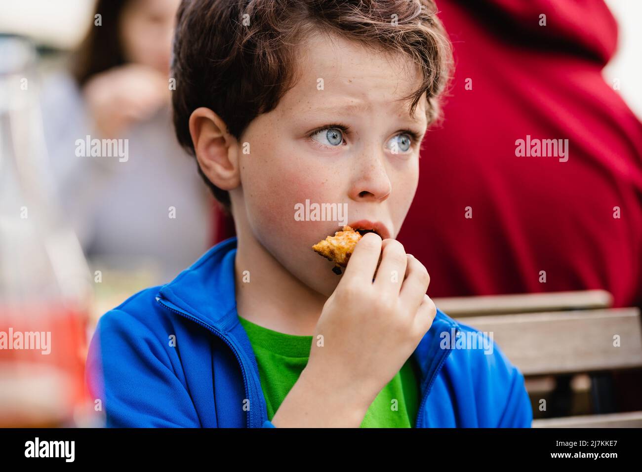 Little boy biting delicious pizza while sitting at table during lunch ...