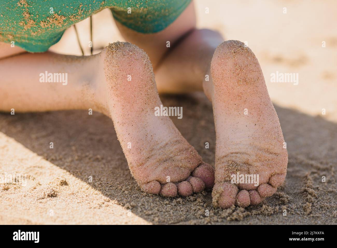 Legs of crop faceless kid covered with sand sitting on beach with ...