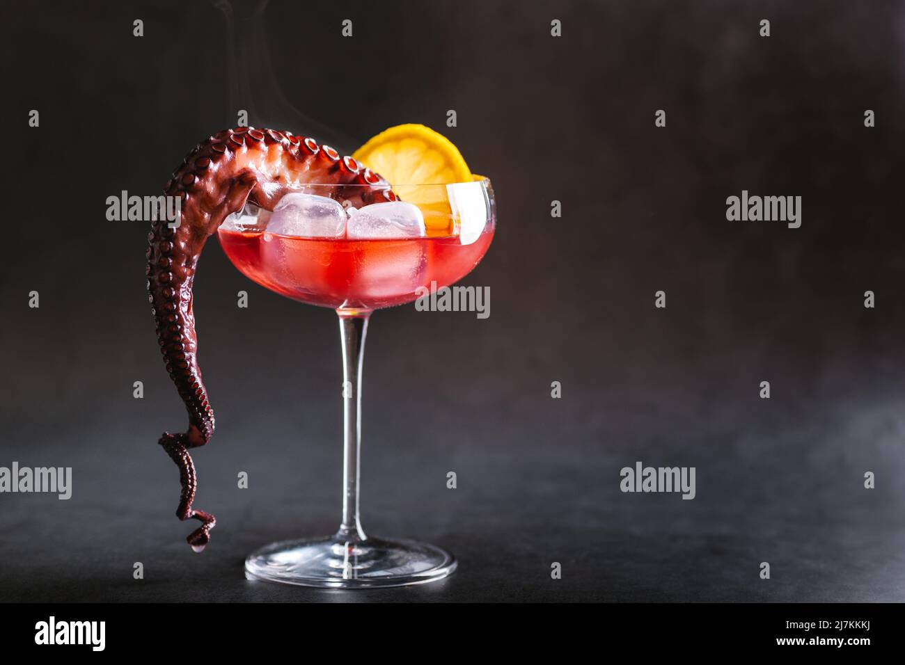 Alcoholic cocktail with ice cubes served with octopus tentacle and ...