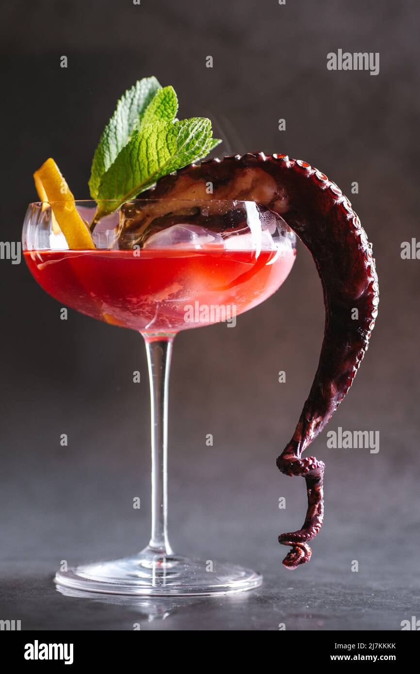Alcoholic cocktail with ice cubes served with octopus tentacle and ...