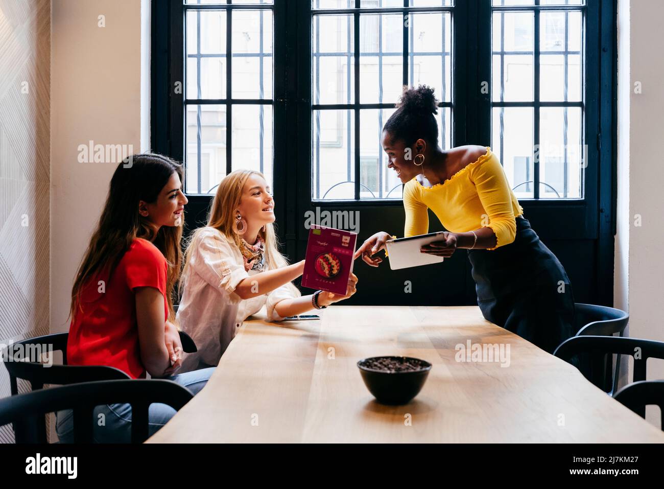 Pretty smiling African American young waitress taking order from modern ...