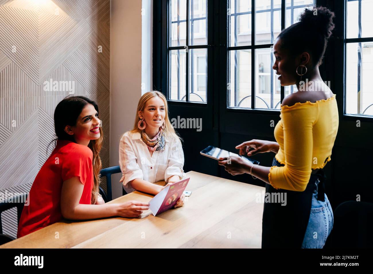 Pretty smiling African American young waitress taking order from modern ...