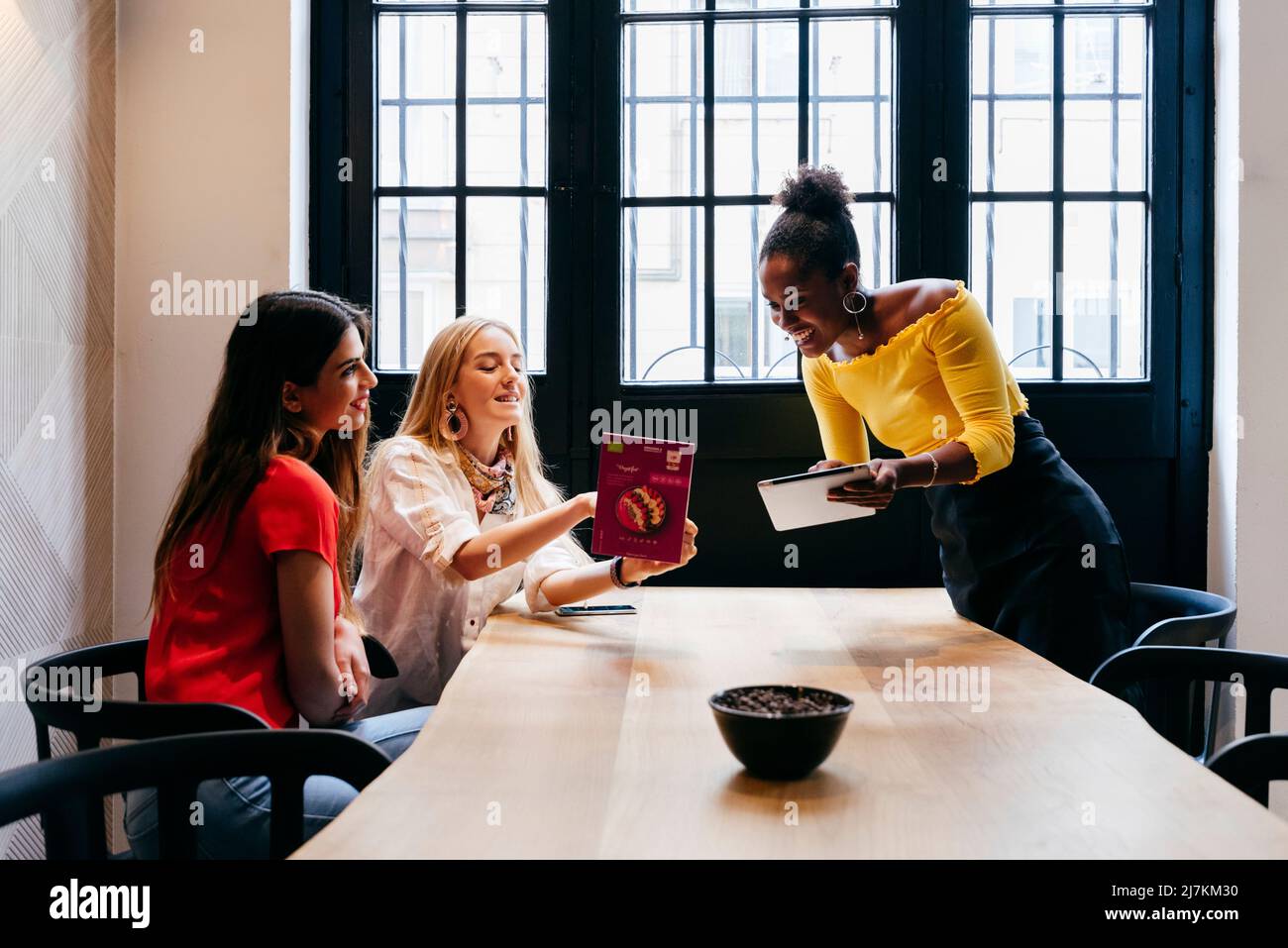 Pretty smiling African American young waitress taking order from modern ...