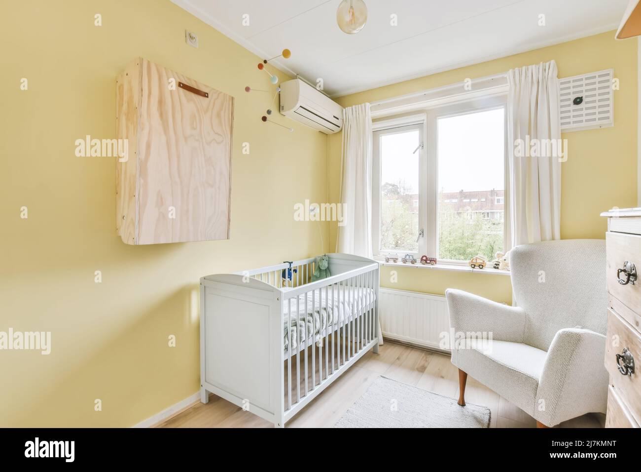 White crib with comfortable big armchair placed near window with toys ...