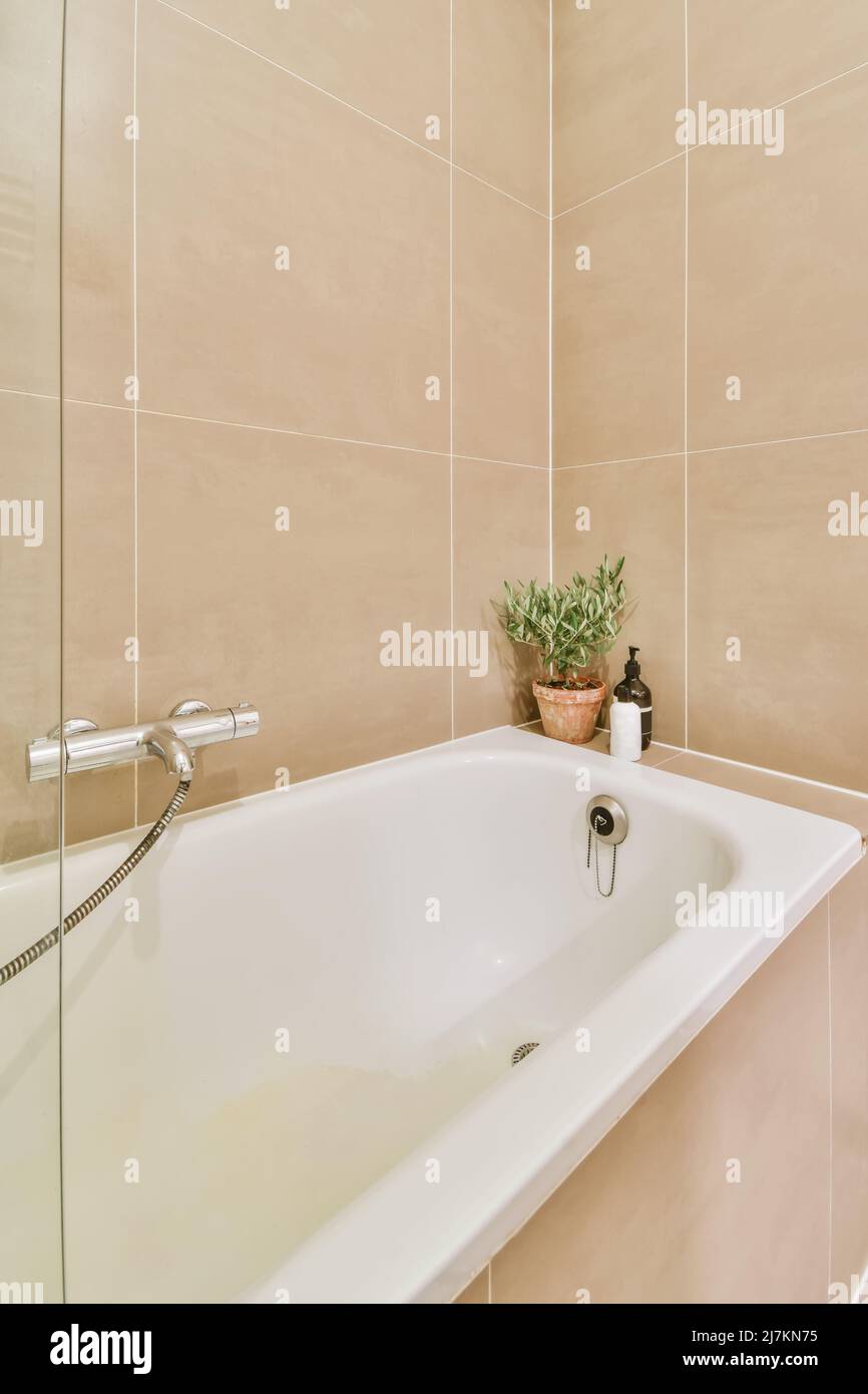 Ceramic bathtub in contemporary bathroom with beige tiled wall with ...
