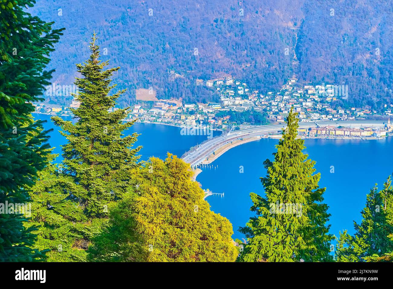 The top view of Lake Lugano and Melide Causeway through the tall green ...