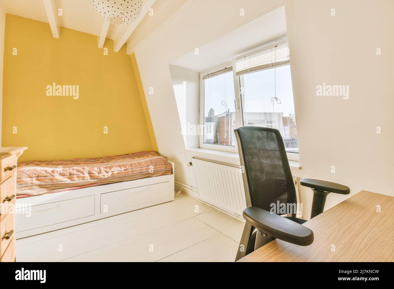 Comfortable bed placed near secretary desk with chair in light spacious ...