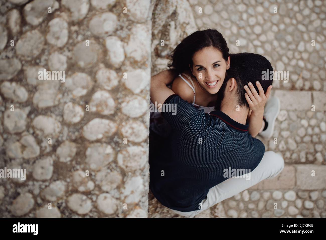 Playful casual couple cuddling and sitting on cobbled city street on ...