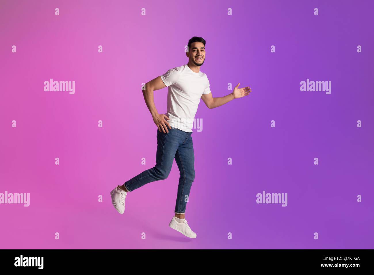 Full length of happy young Arab man in t-shirt and jeans running in ...