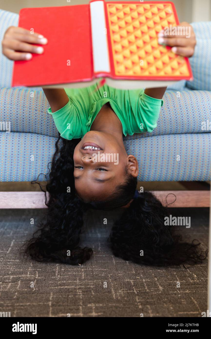 Smiling african american elementary girl reading book while lying ...
