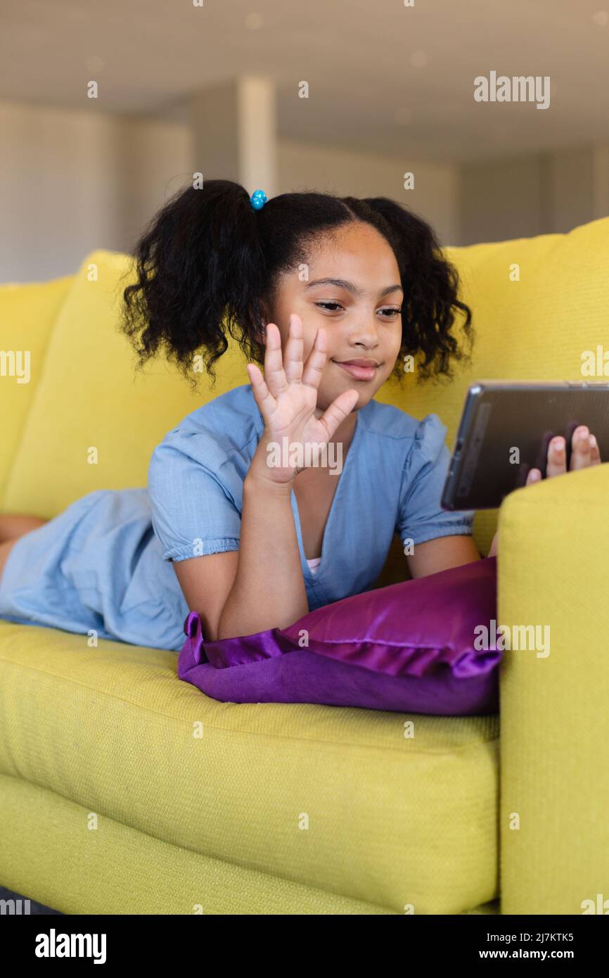 Biracial elementary girl waving over smart phone during video call ...